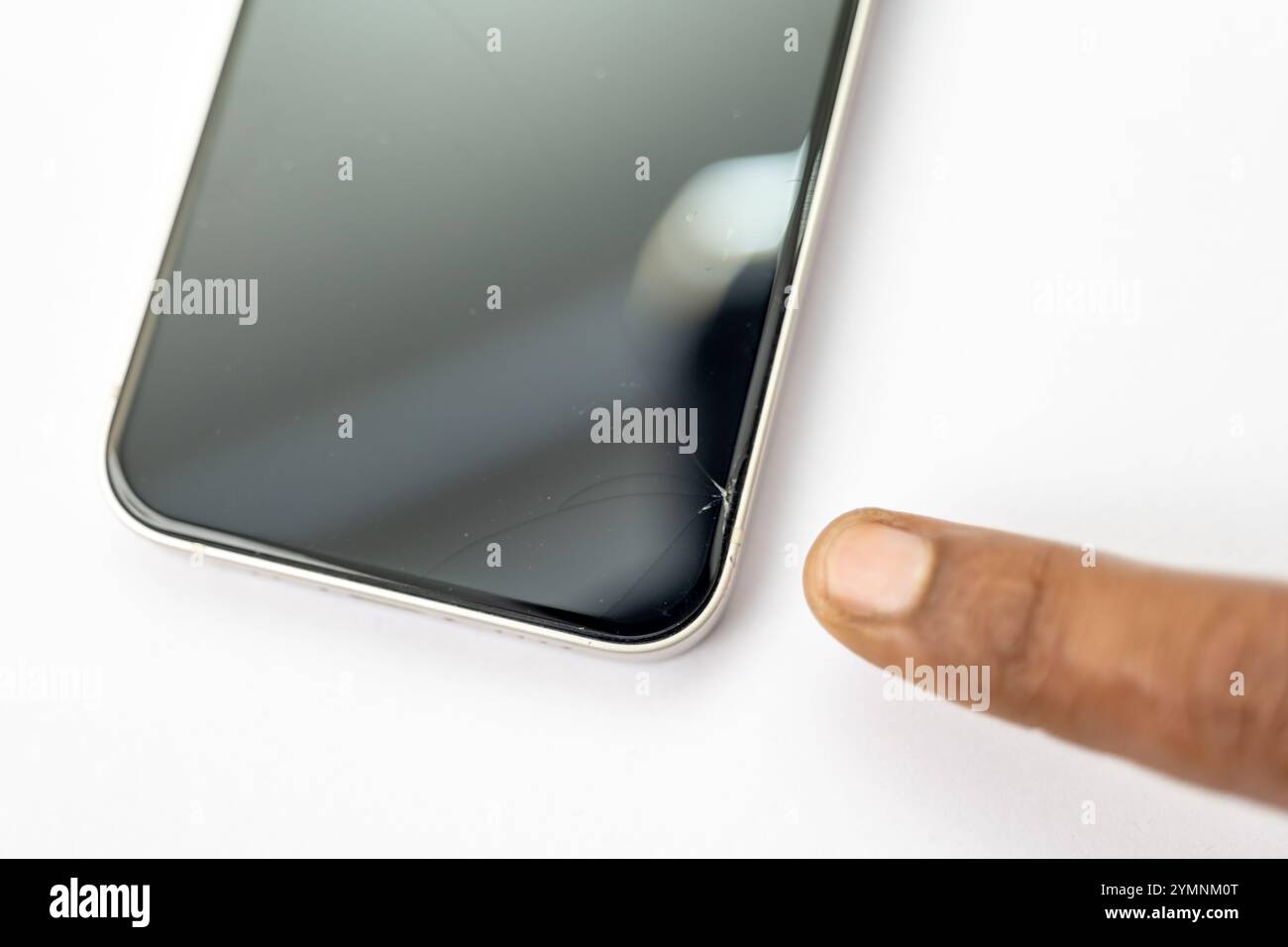 Close-up of a finger pointing at a cracked smartphone screen on a white ...