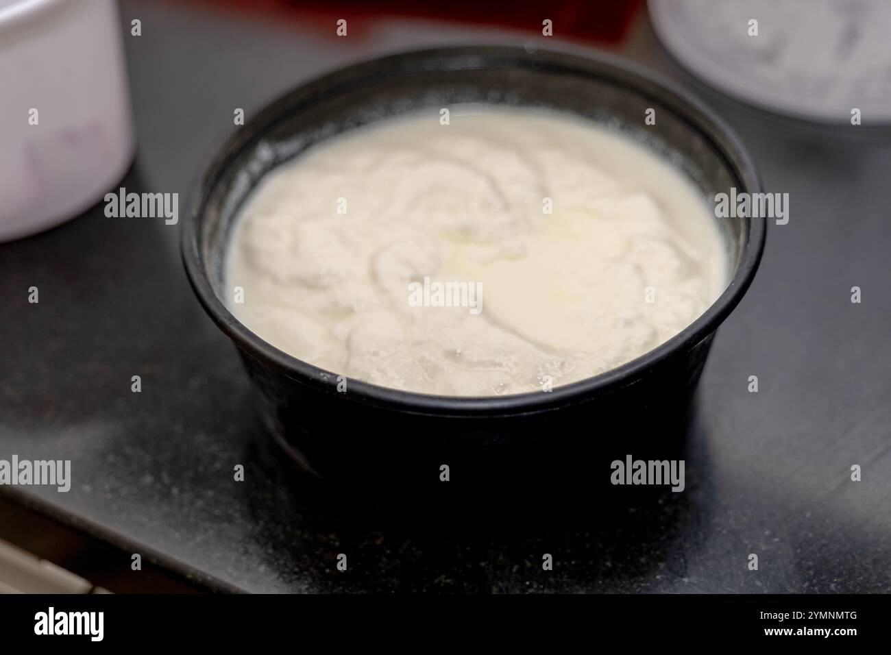 Creamy homemade cheese curds separating from whey in a black bowl. A ...