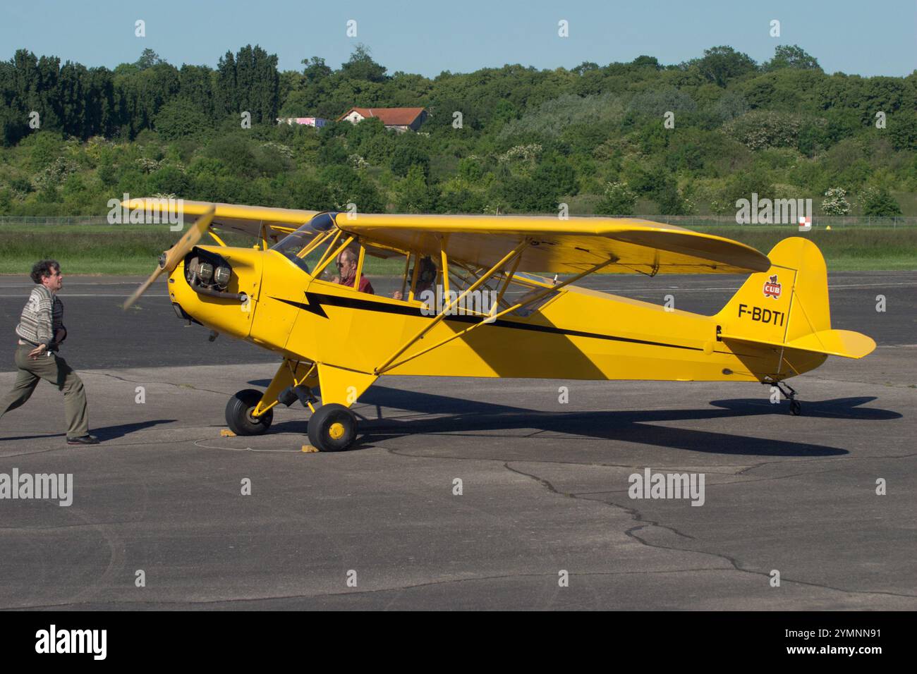Man swinging the wooden propeller of a vintage yellow Piper J-3 Cub ...