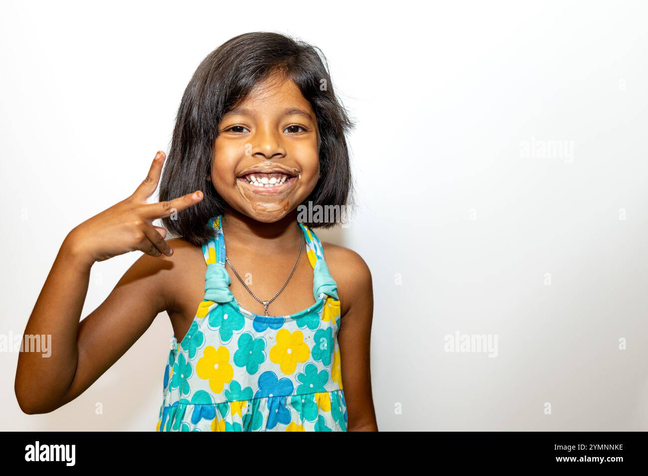 Adorable girl with chocolate around her mouth gives a peace sign ...