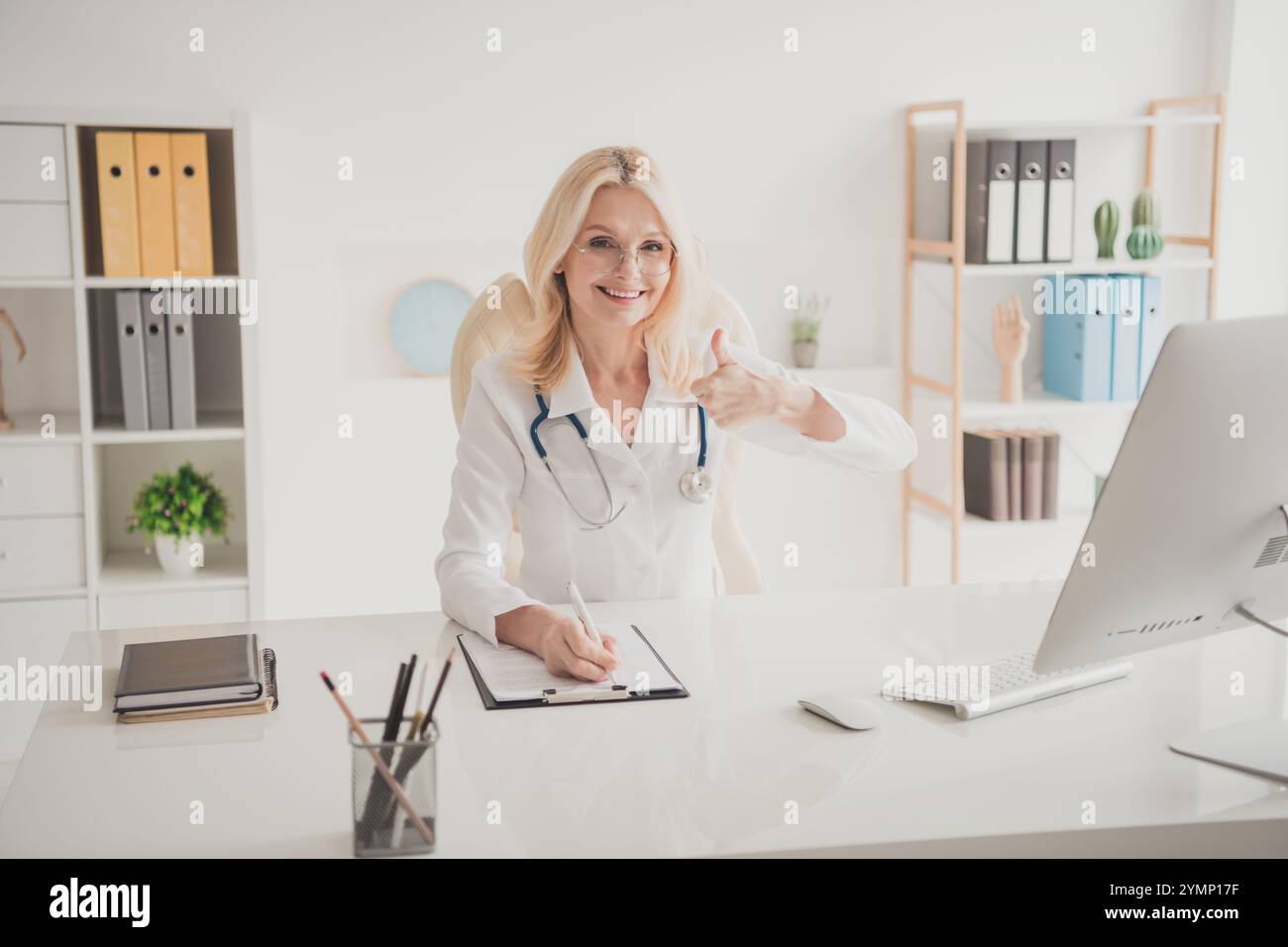 Confident senior female doctor in a clinic office offering a thumbs-up ...