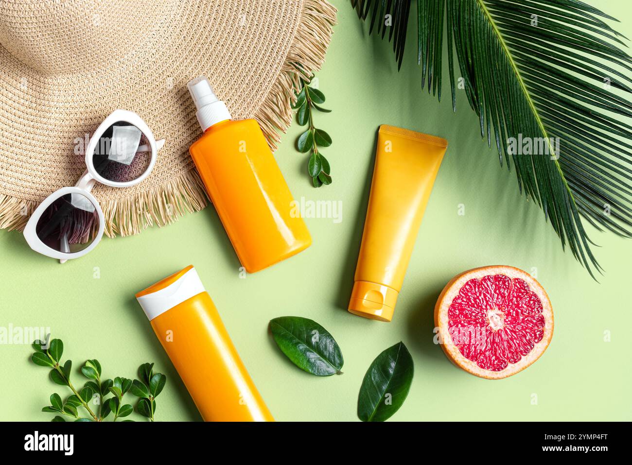 Orange sunblock package, sunglasses, straw hat and palm leaves on green ...