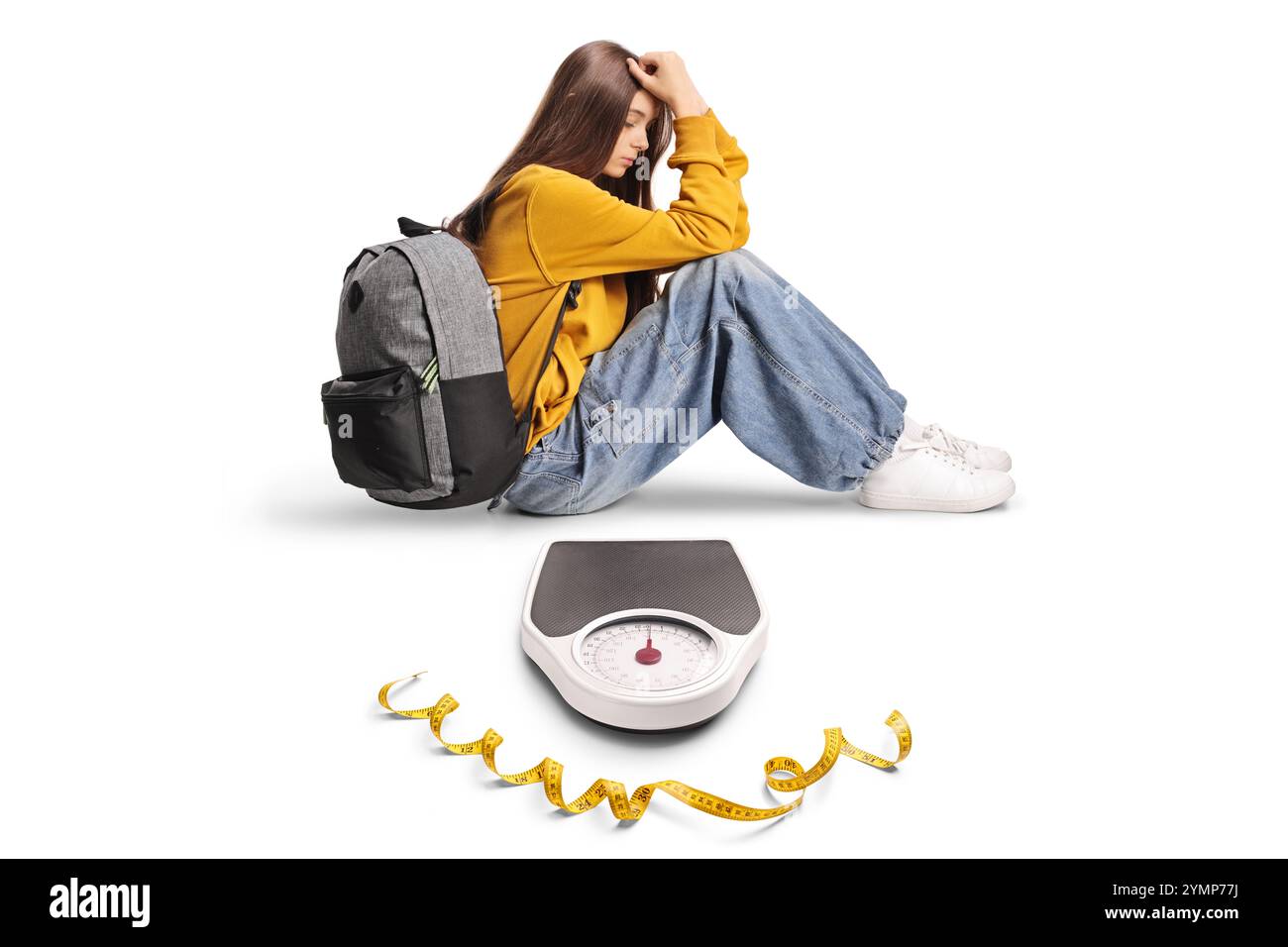 Sad female student sitting on the ground next to a weight scale ...
