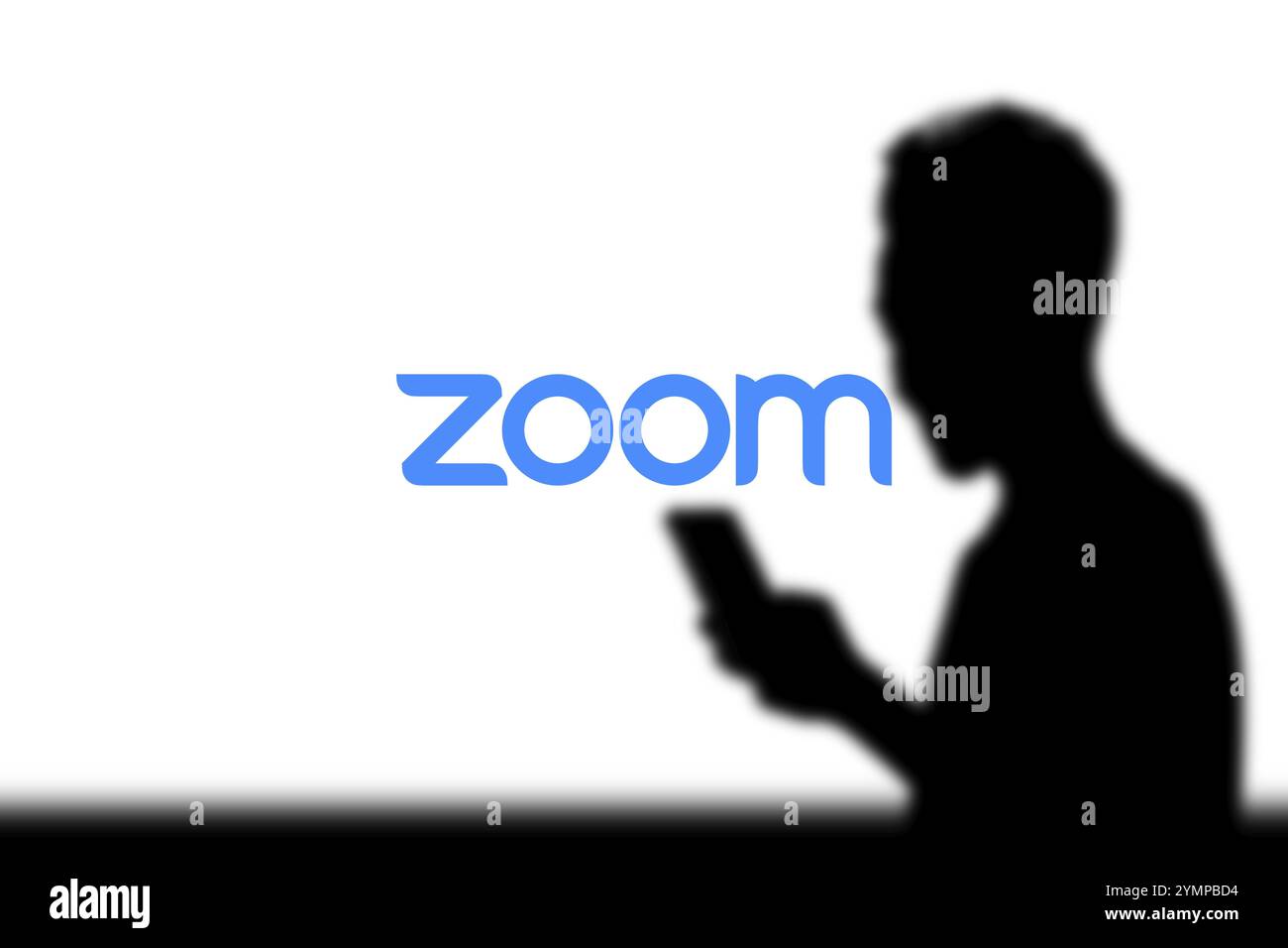 Zoom App logo on smartphone screen while Zoom meeting in the background ...