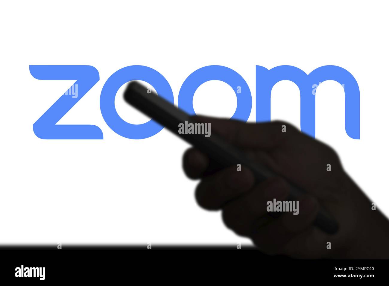 Zoom App logo on smartphone screen while Zoom meeting in the background ...