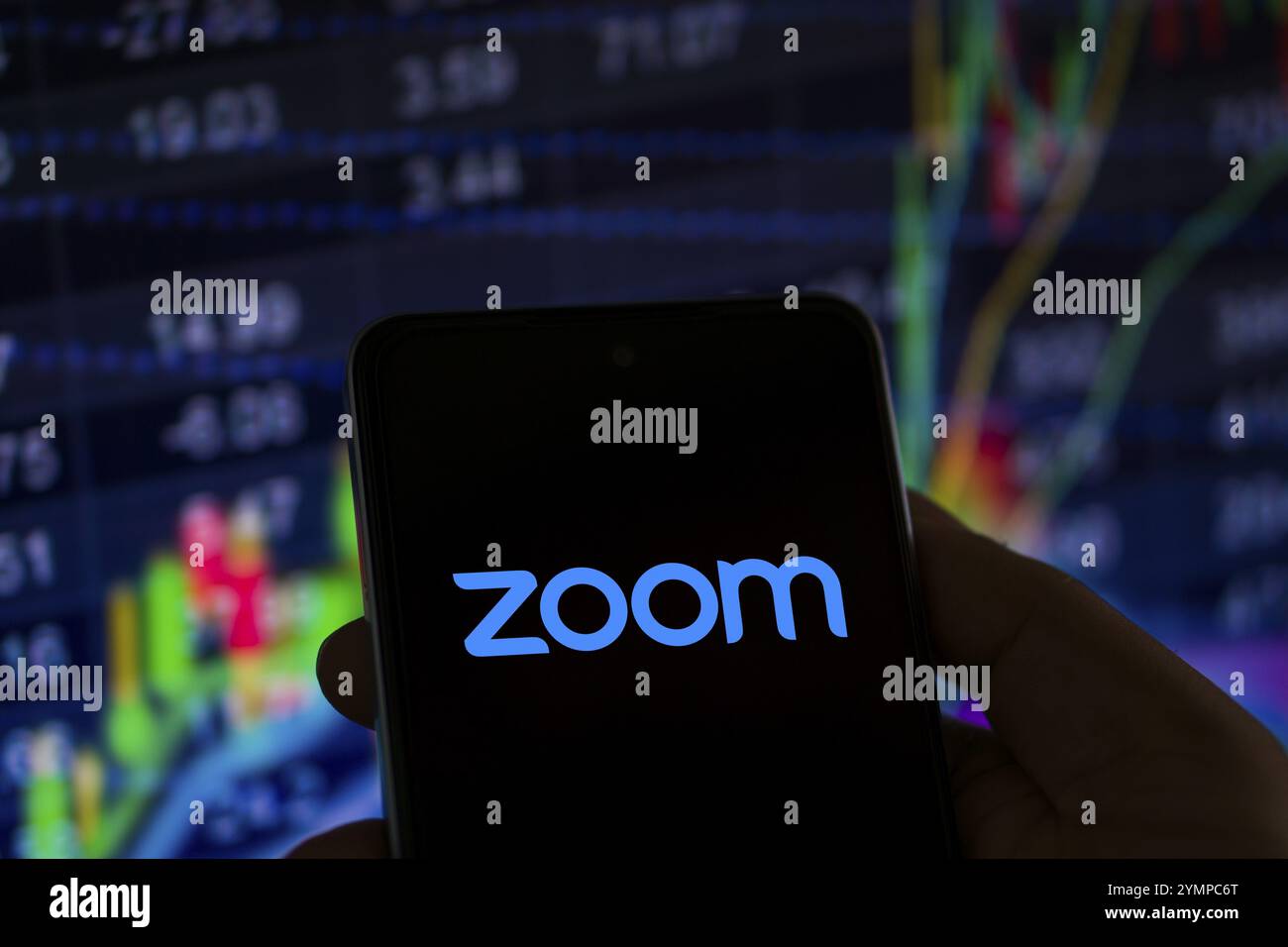 Zoom App logo on smartphone screen while Zoom meeting in the background ...