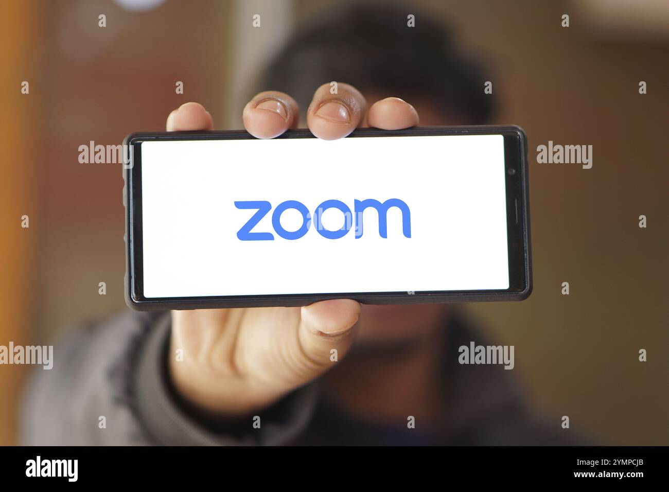 Zoom App logo on smartphone screen while Zoom meeting in the background ...