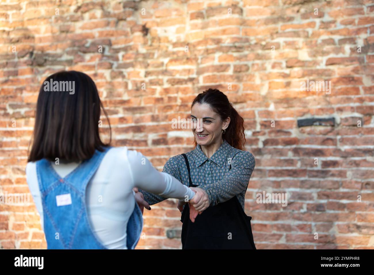 Two women holding hands and smiling in front of a brick wall, enjoying ...