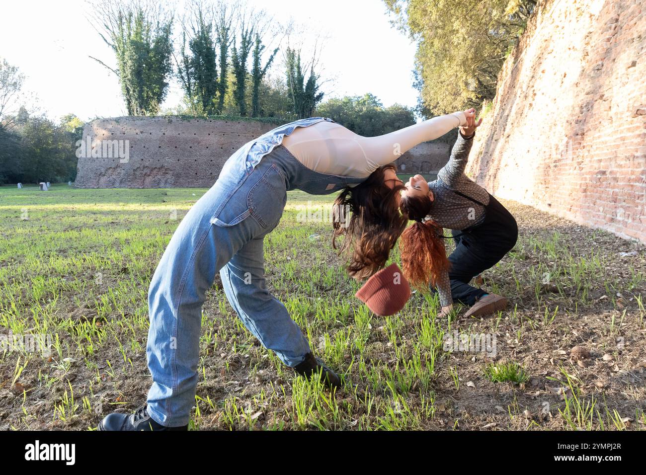 Two female dancers performing acrobatic movements in a park, bending ...