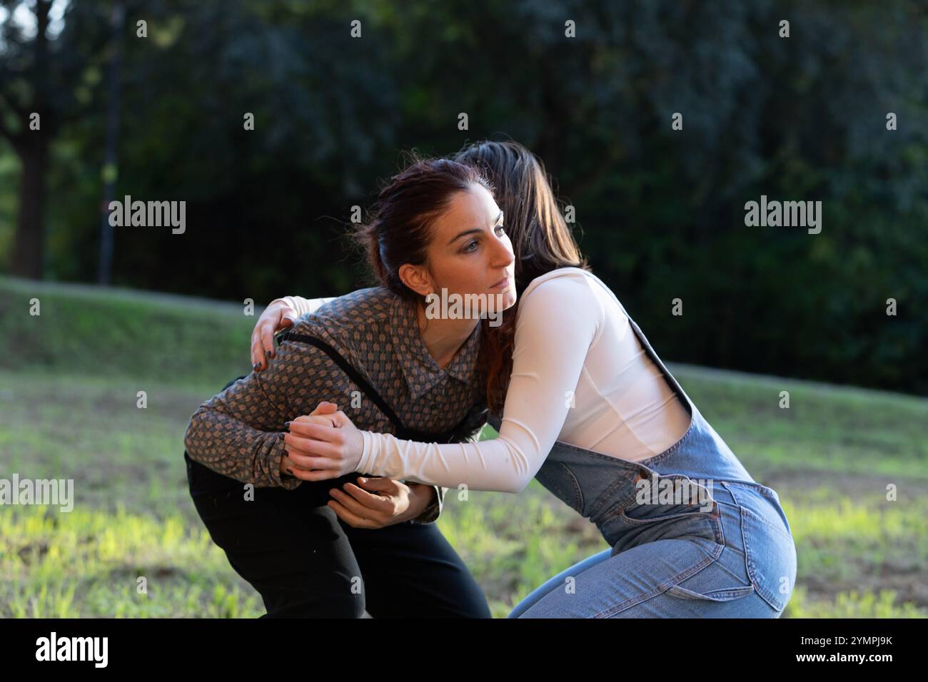 Two young women are embracing in a park, conveying feelings of support ...