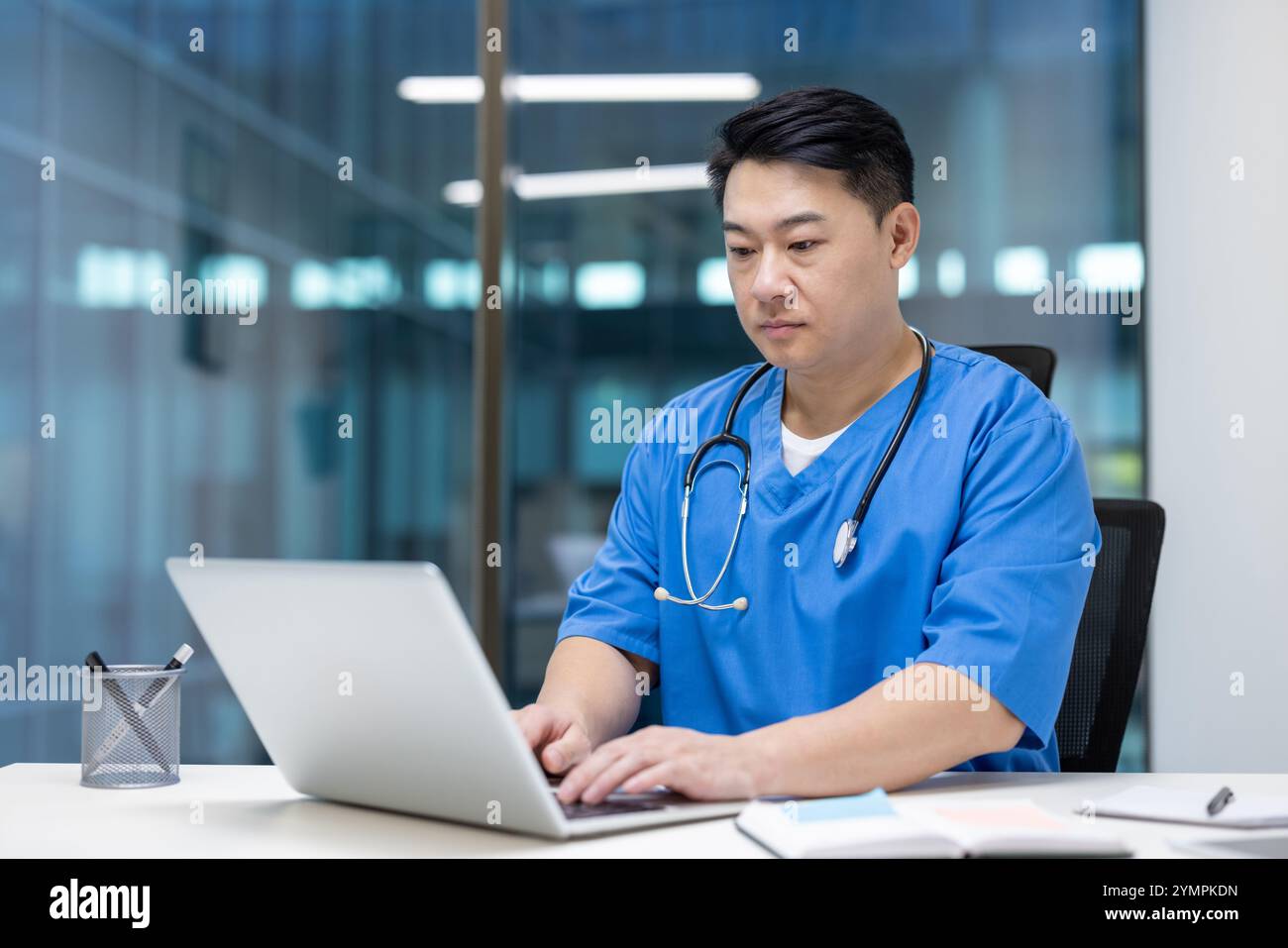 Asian man doctor wearing blue scrubs with stethoscope works at modern ...