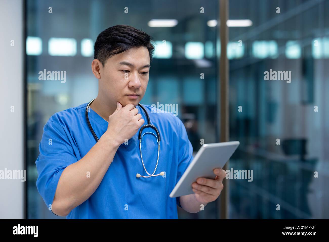 Asian man doctor wearing blue scrubs uses digital tablet in modern ...