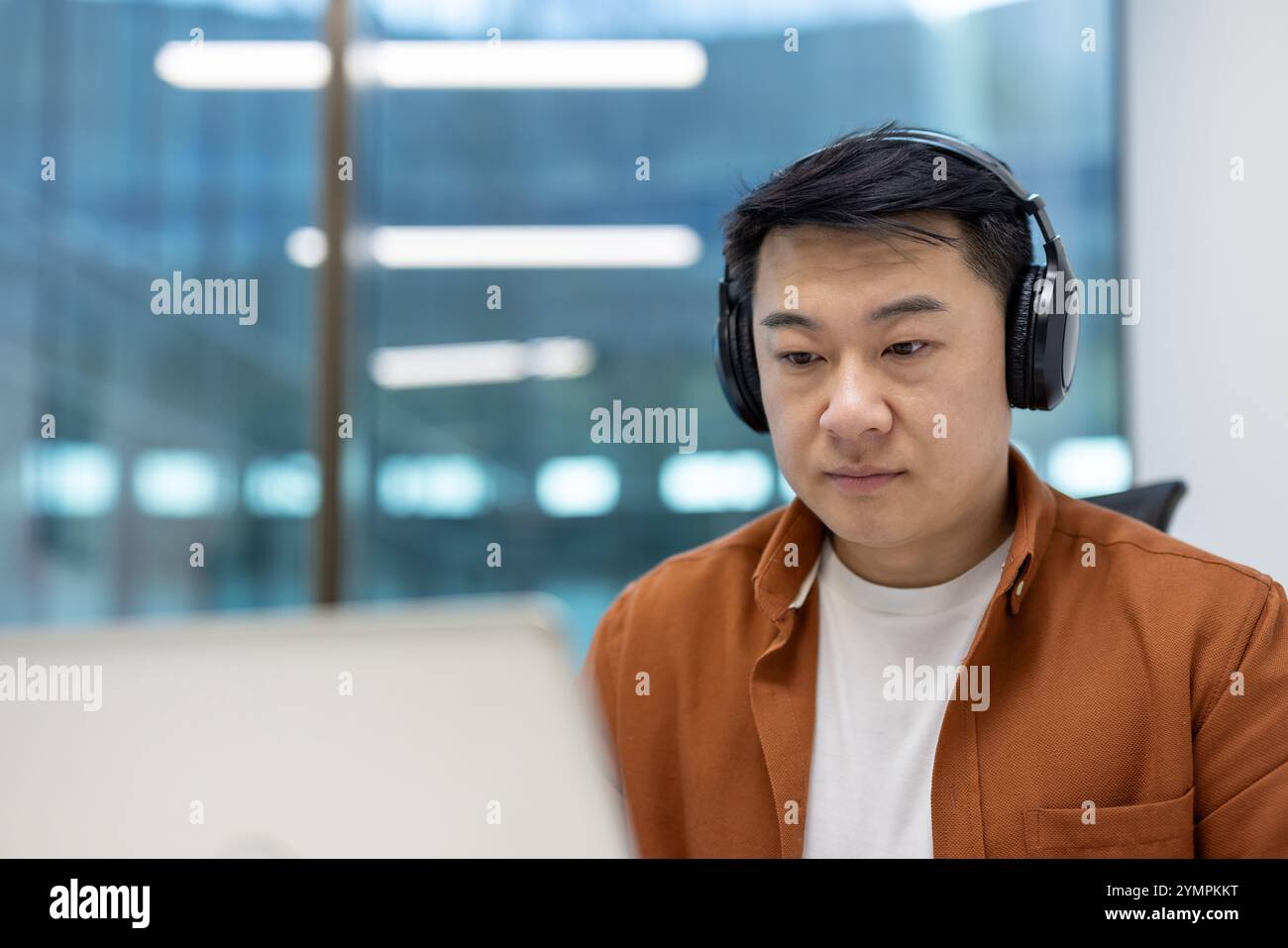 Asian man businessman wearing headphones focused on laptop. Reflects ...