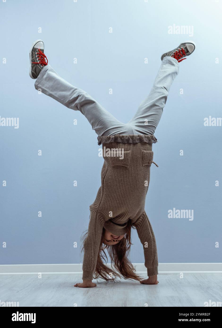 Young girl with long brown hair is doing a handstand, wearing a brown ...