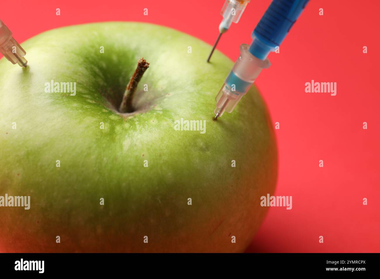 GMO concept. Green apple with different syringes on red background ...