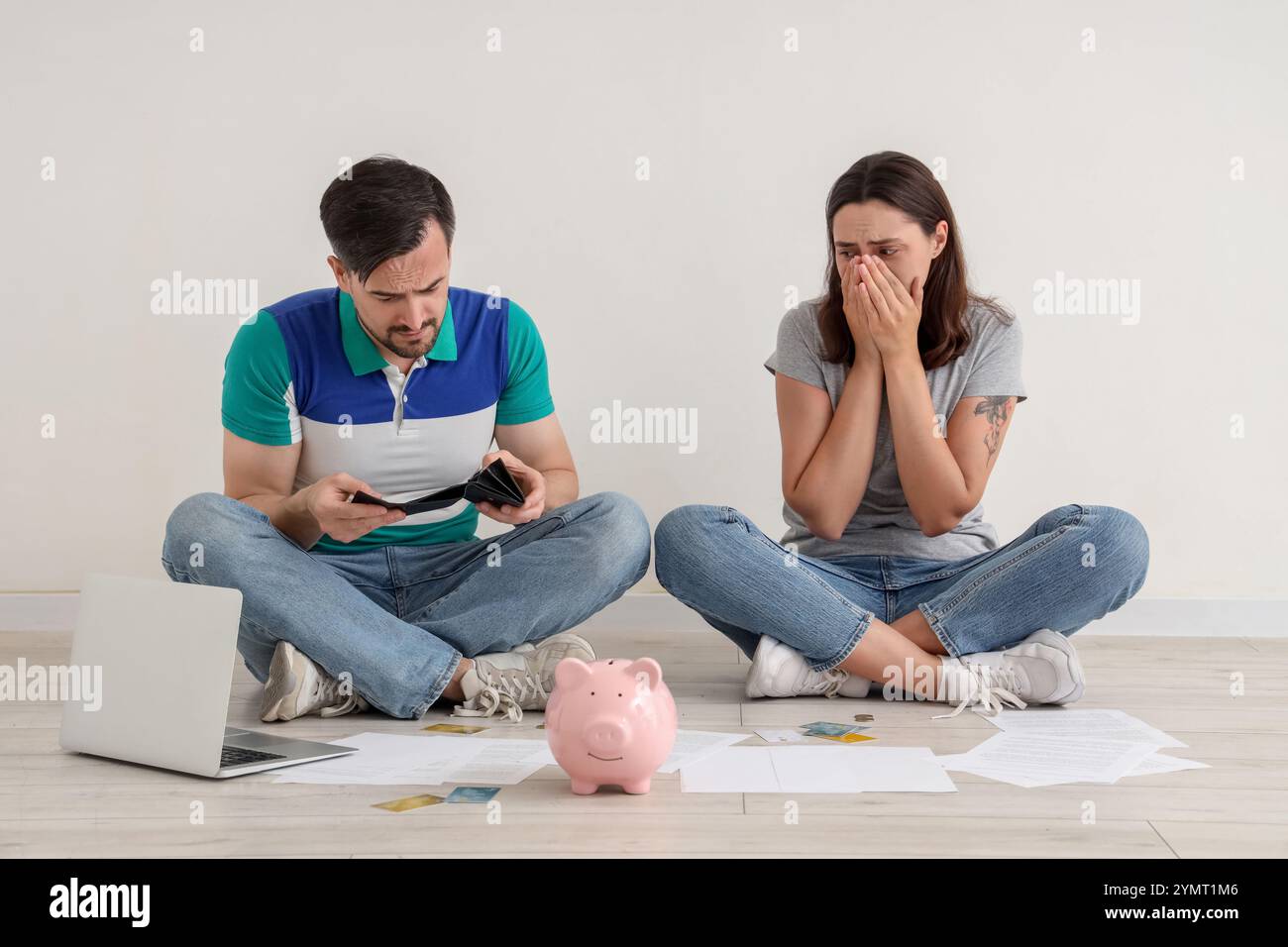 Young man looking into his empty wallet while his wife crying on floor ...