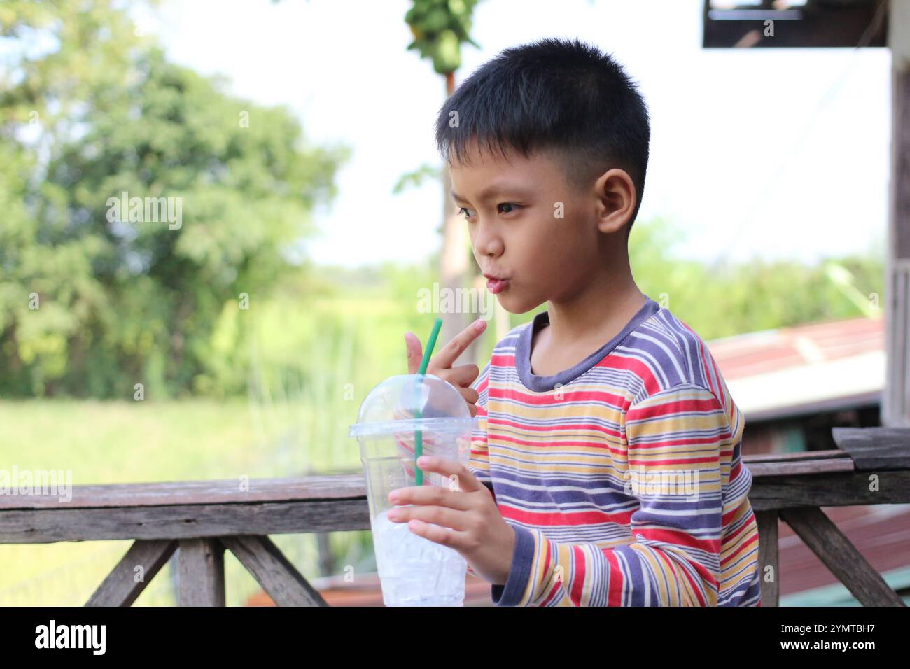 A young boy sits outdoors, sipping a cool drink with a straw. His ...