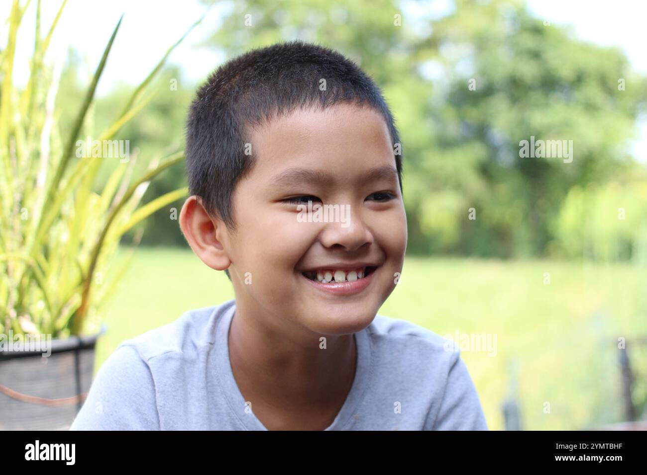A joyful young boy smiles brightly in a natural outdoor setting ...