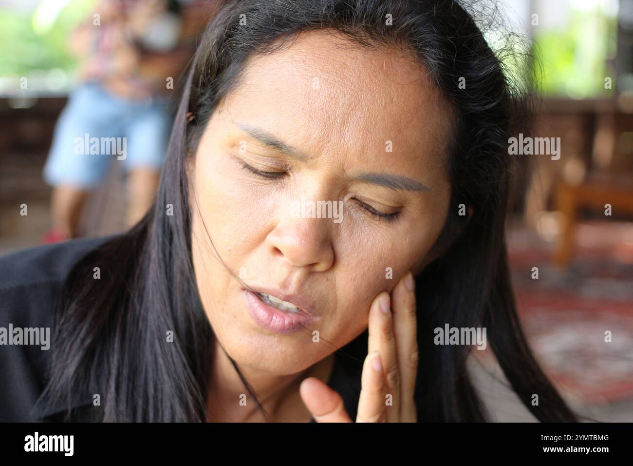 A woman shows discomfort while holding her jaw, expressing pain and ...