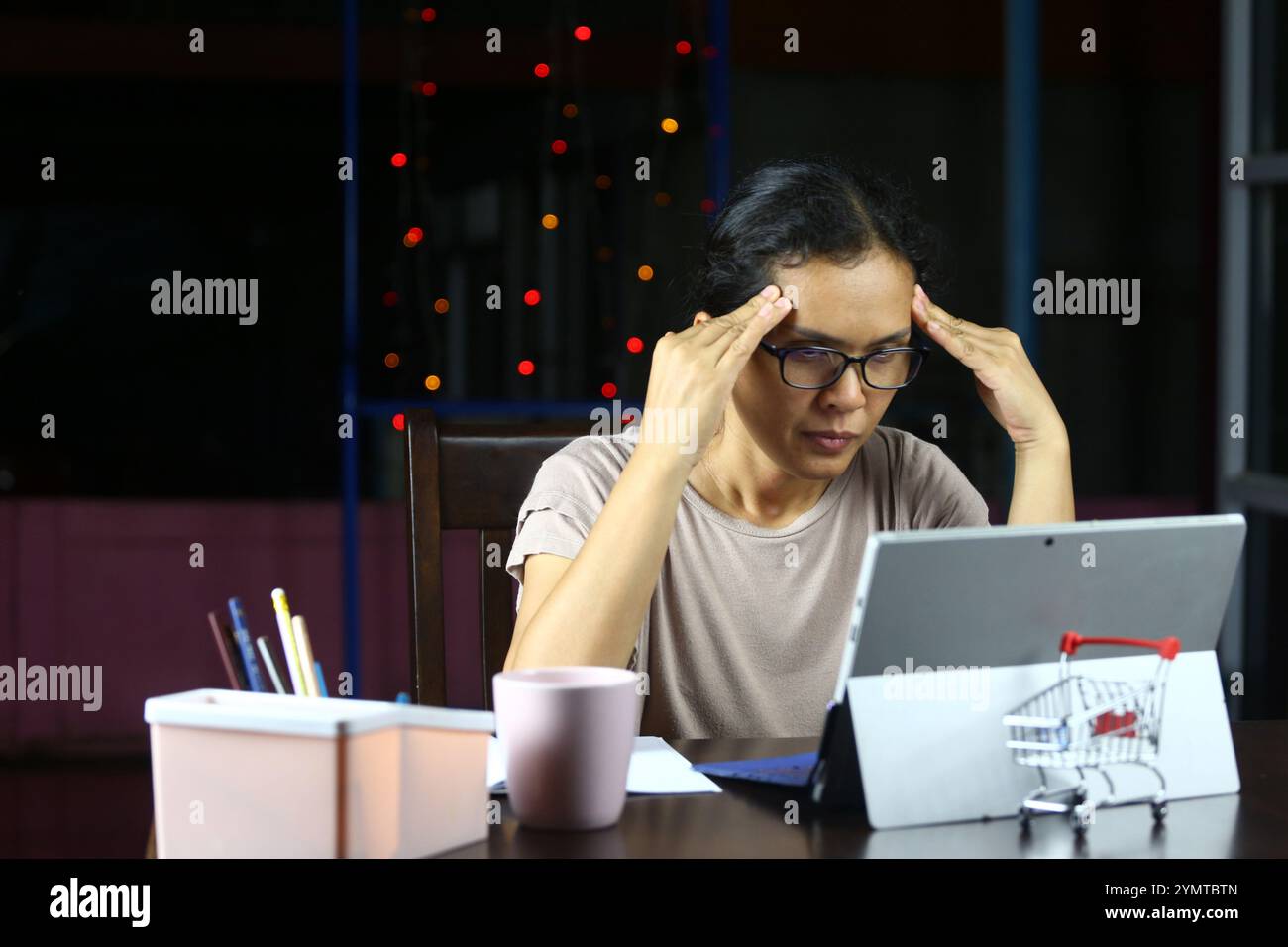 A woman sits at her desk with a tablet, displaying signs of stress and ...