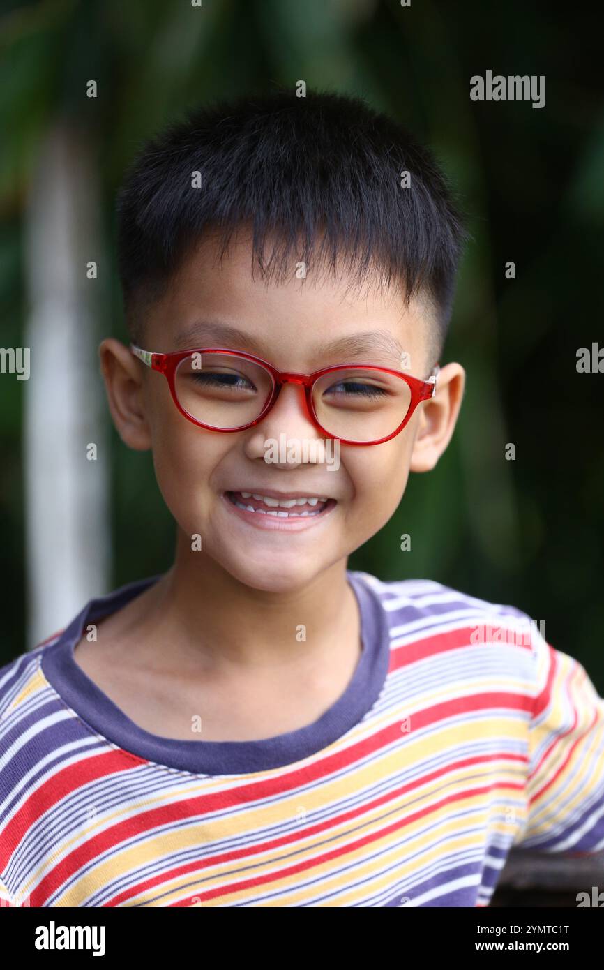 A cheerful boy with glasses smiles broadly while wearing a colorful striped shirt. The image ...