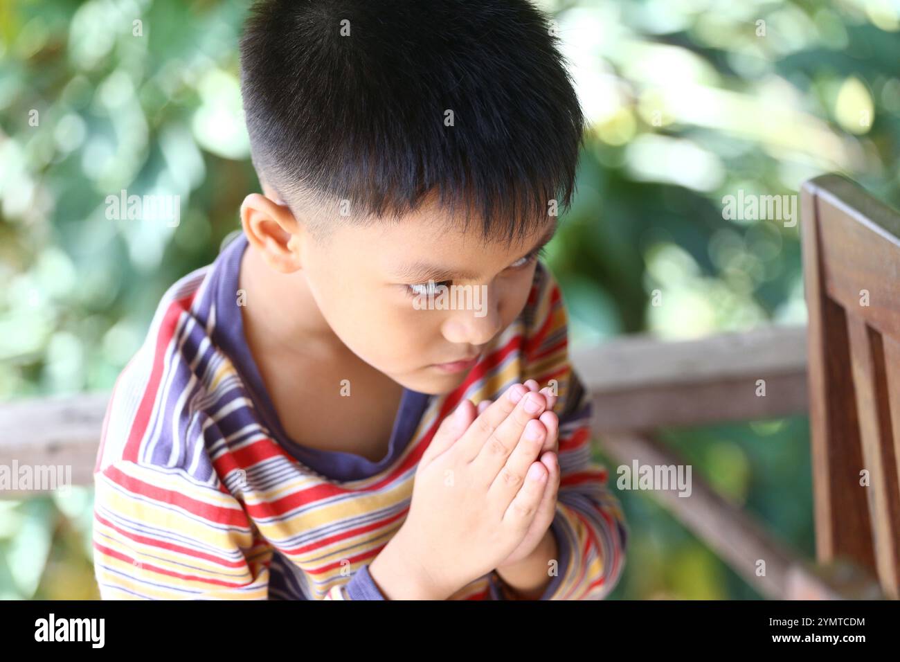 A young boy is seen outdoors with his hands in a prayer position ...
