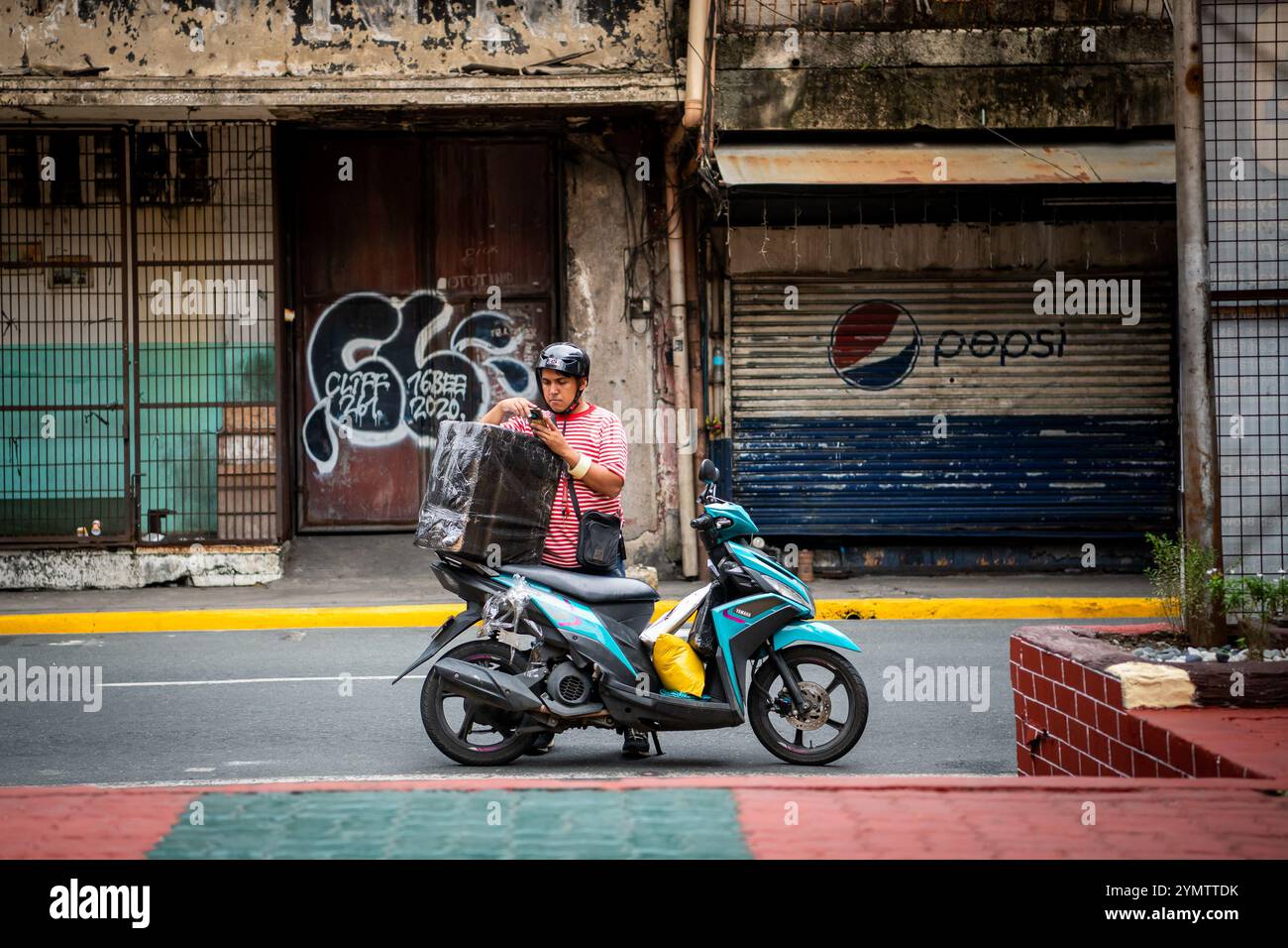 A Filipino man packs up a large case on his moped in the Ermita area of ...