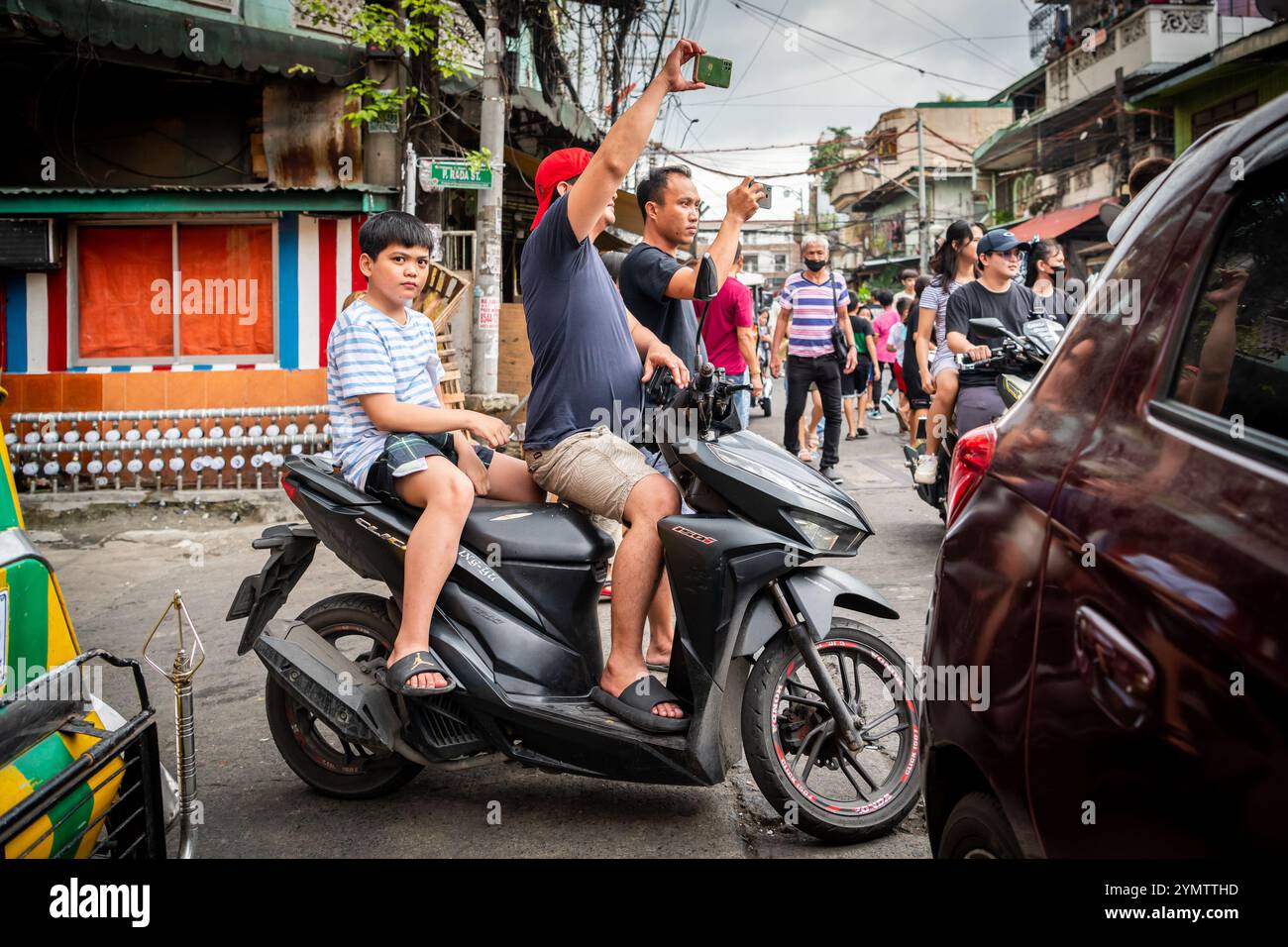A young Filipino boy gets a ride on the back of a motorbike through the ...