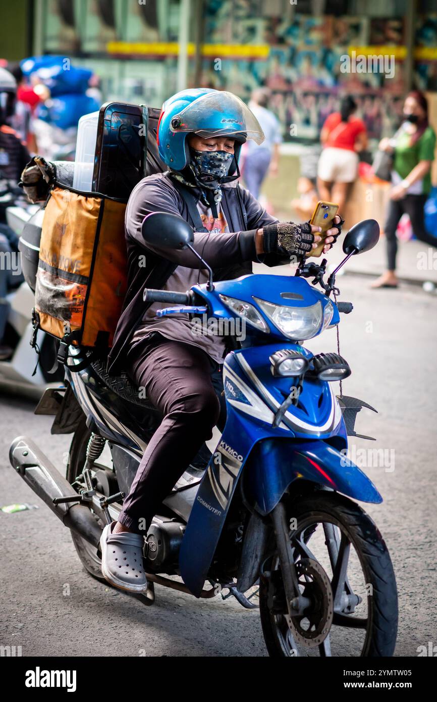A Filipino bike courier takes a break to check his phone on the busy streets of Manila, The ...