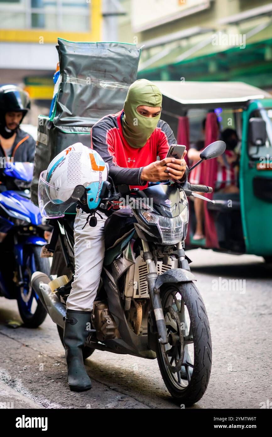 A Filipino bike courier takes a break to check his phone on the busy streets of Manila, The ...