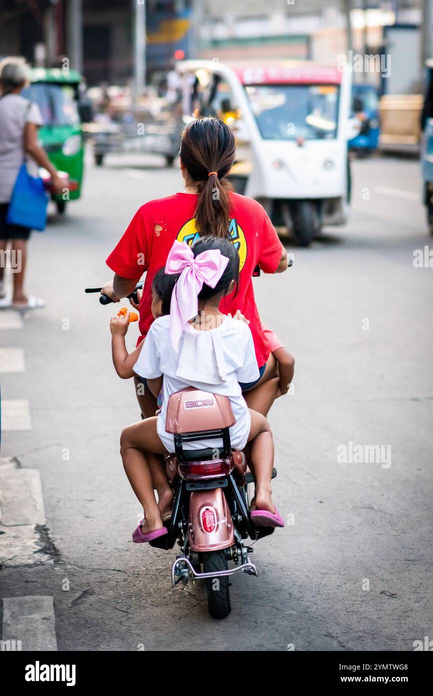 Two young Filipino children sat on mums bike get taken through the busy ...