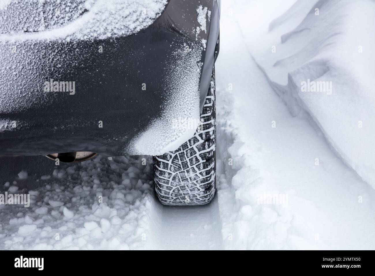 Thick layer of snow on winter road. Rear bumper and car wheel with ...