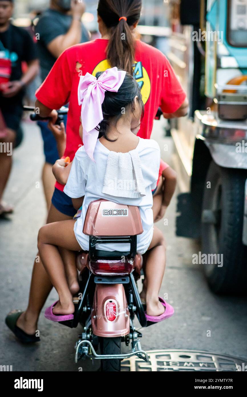 Two young Filipino children sat on mums bike get taken through the busy ...