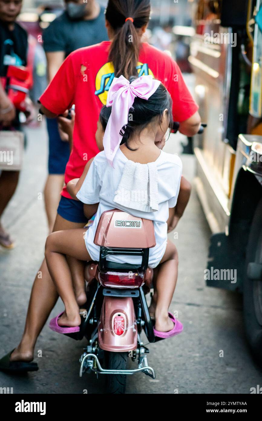 Two young Filipino children sat on mums bike get taken through the busy ...