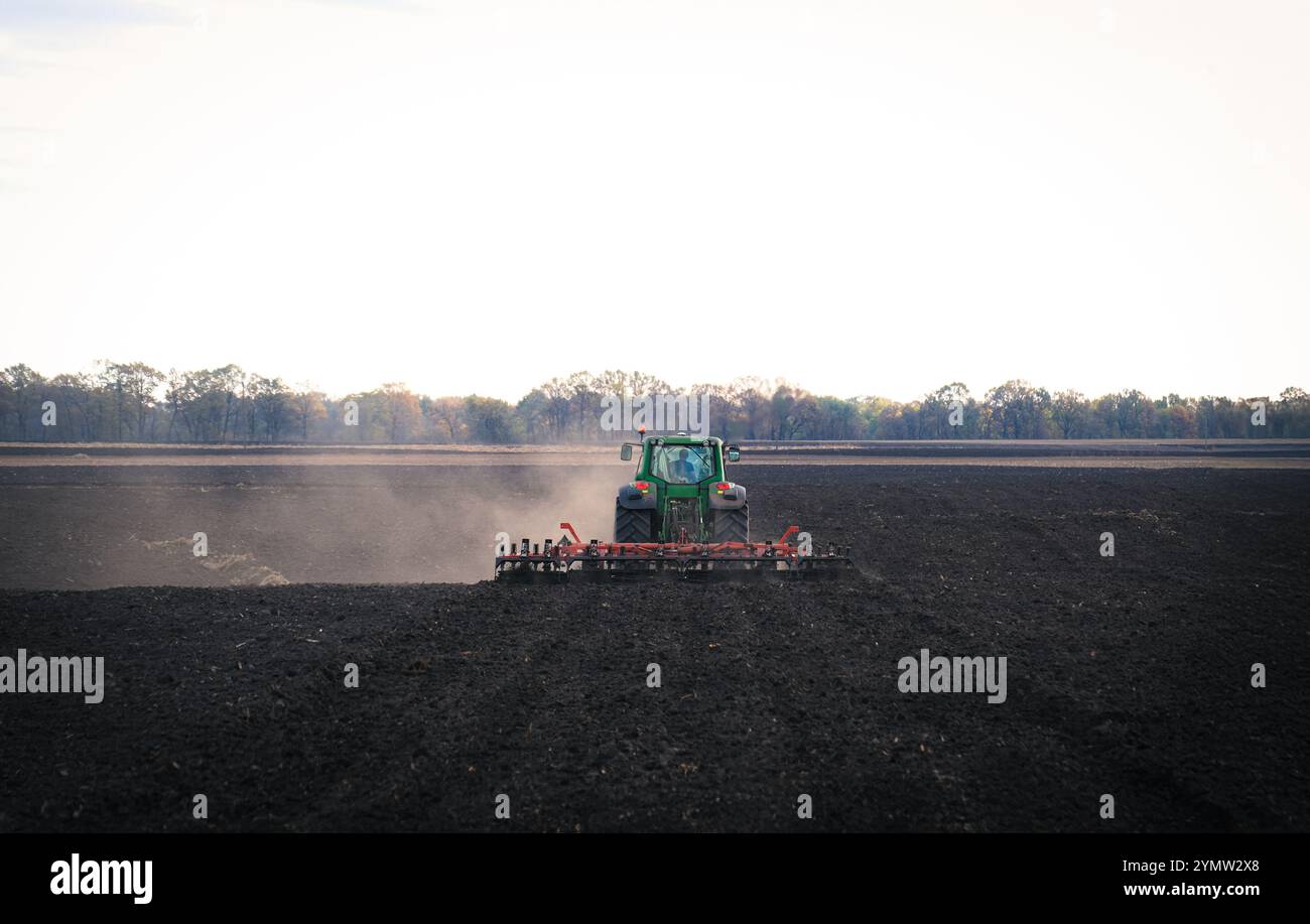 A powerful tractor plows a fertile field, raising clouds of dust ...