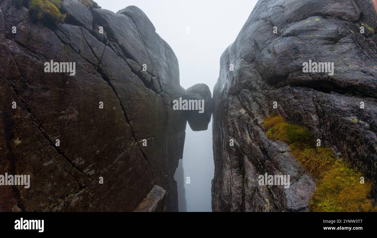 A large boulder wedged between two towering cliffs in a foggy landscape ...