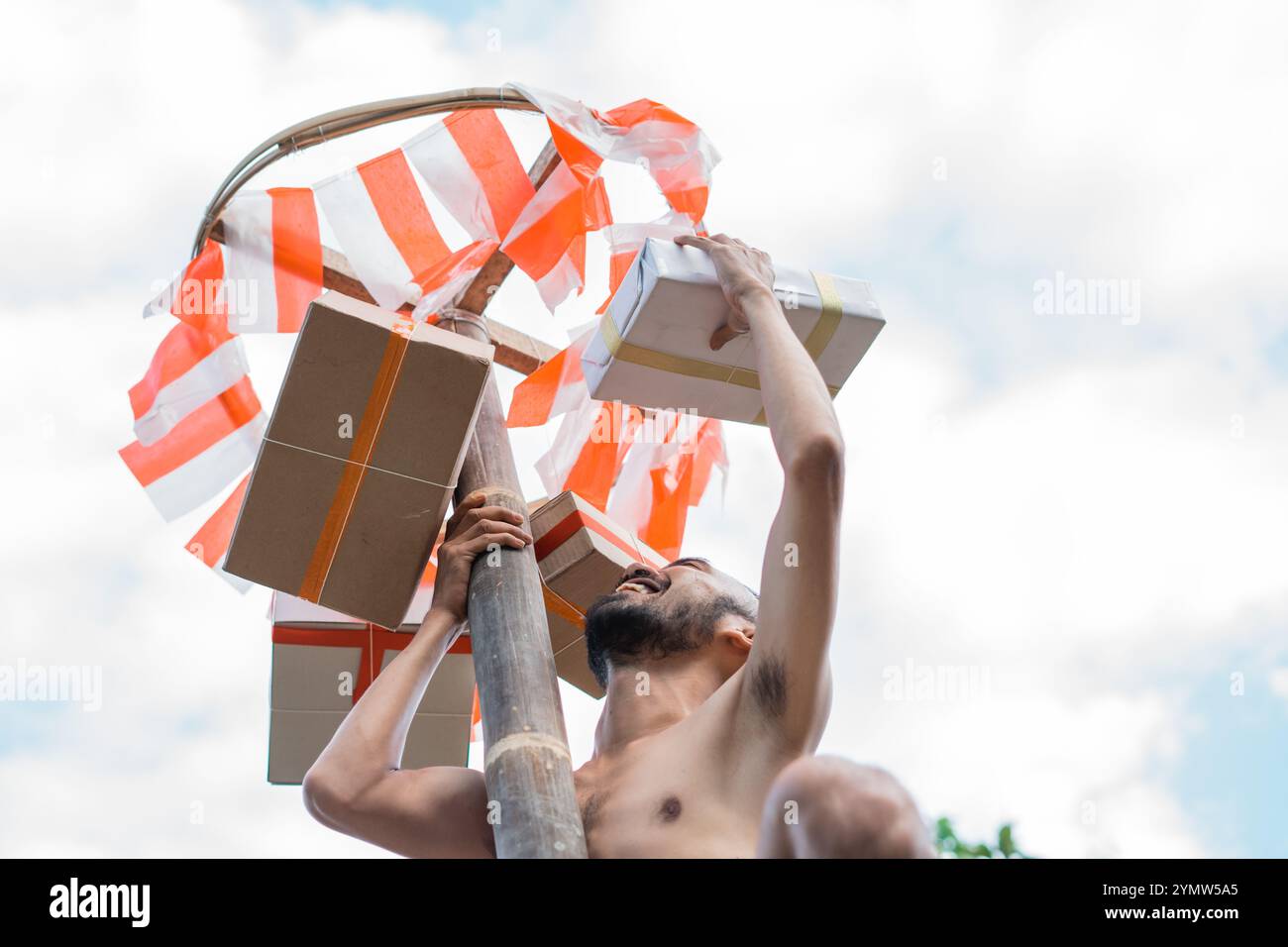man grabs a cardboard box prize during a betel nut climbing competition ...