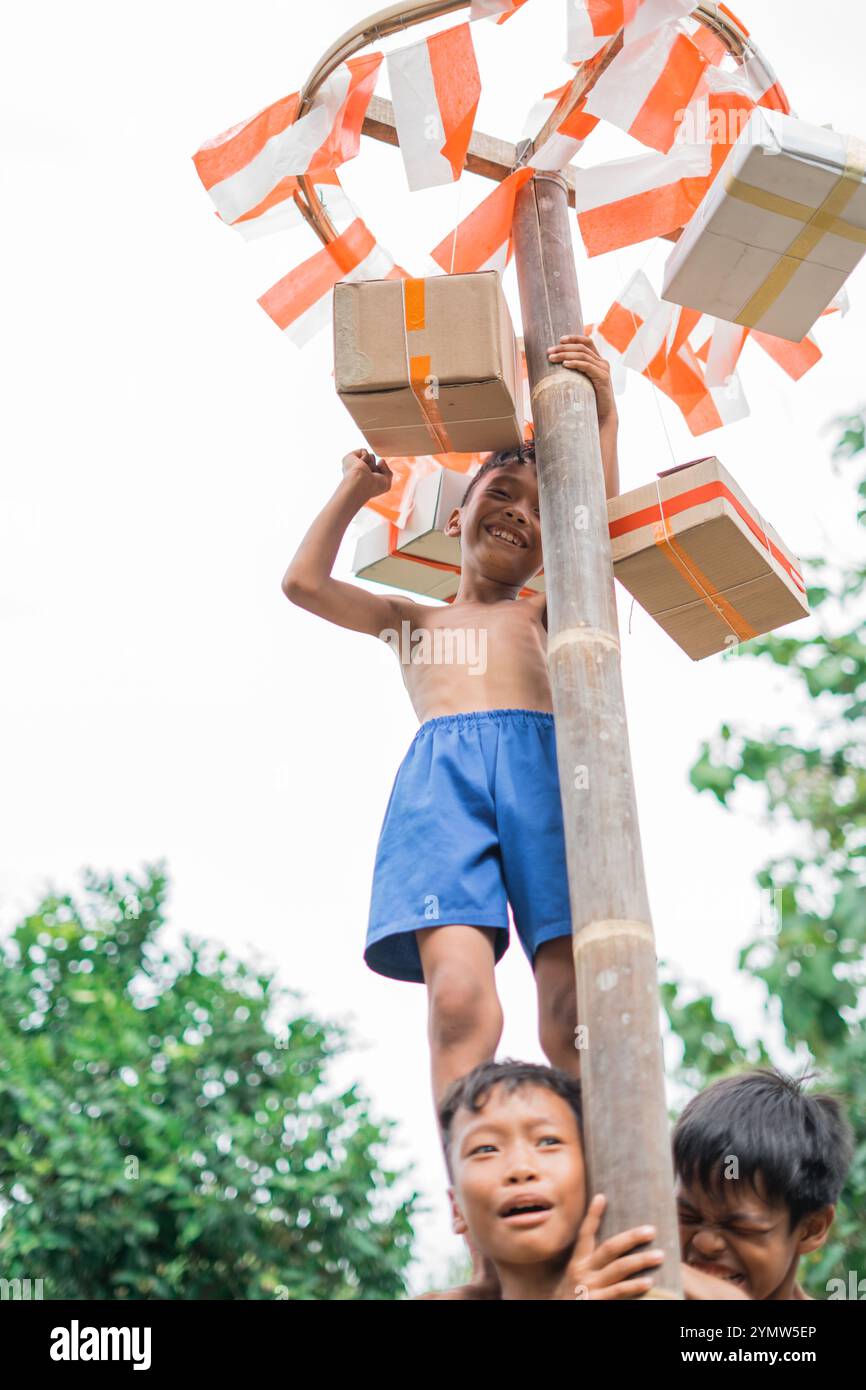 boy standing on friend's shoulder taking prize box hanging during betel ...