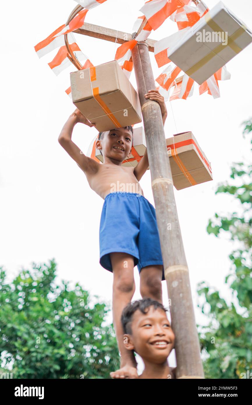boy stands on friend's shoulders reaching for prize during betel nut ...