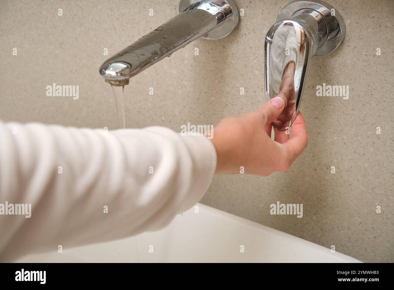 Hand adjusting water faucet handle with water flowing into sink. Close ...