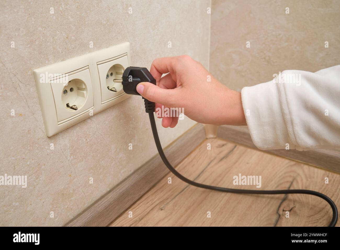 Hand plugging a black electrical plug into a white wall socket. Close ...