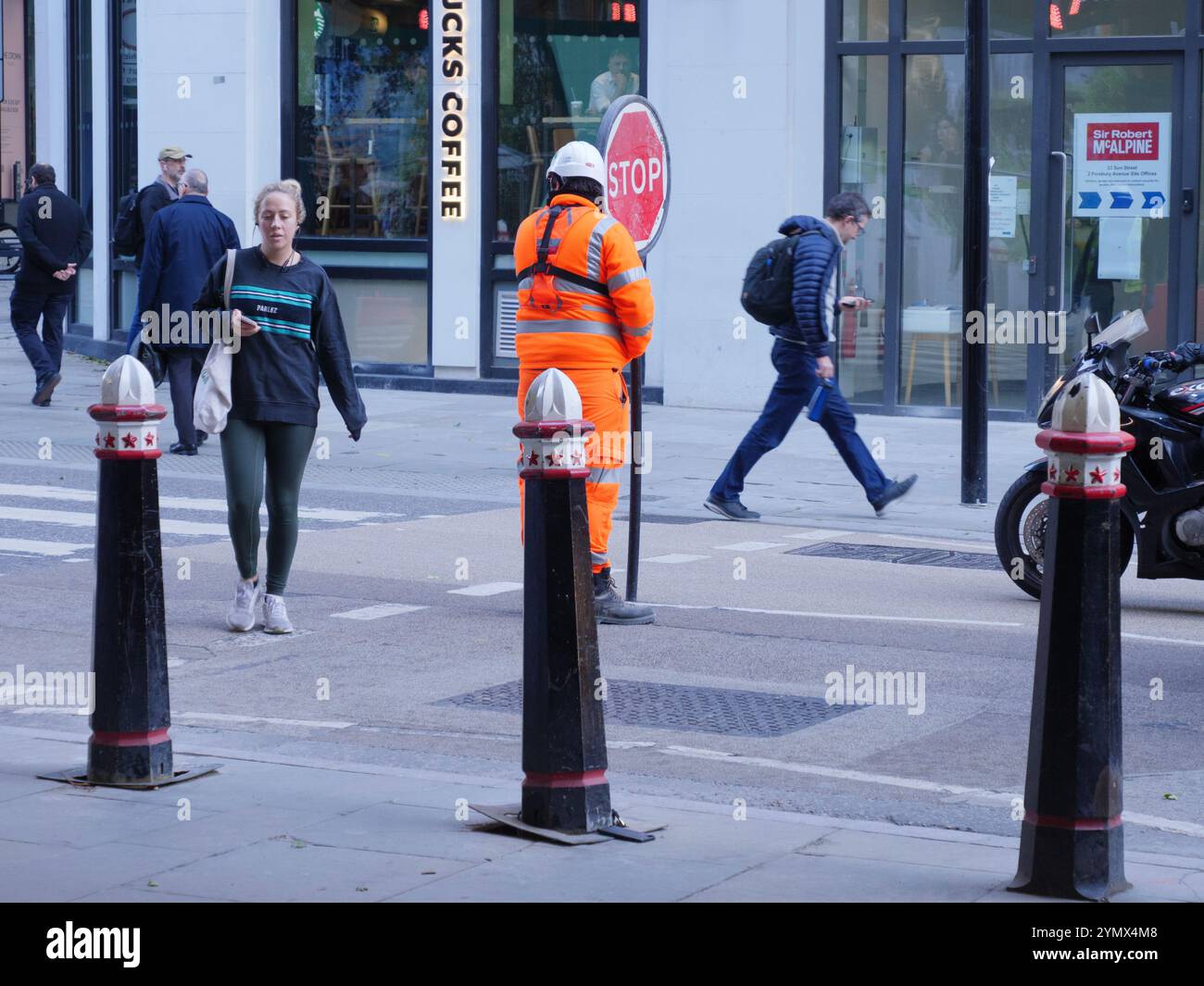 Banksman with stop traffic sign directing pedestrians and traffic at ...