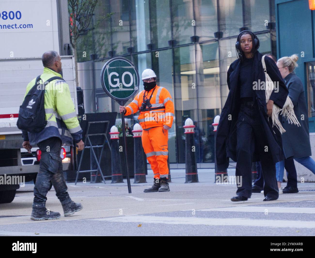 Banksman with go traffic sign directing pedestrians and traffic at ...