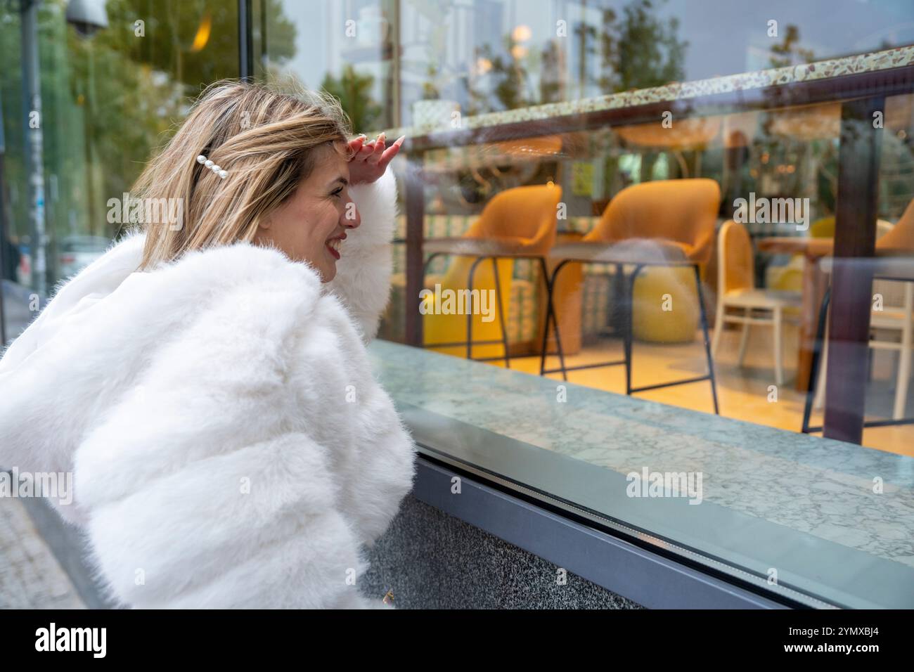 Elegant woman shielding her eyes while looking through a window at a ...