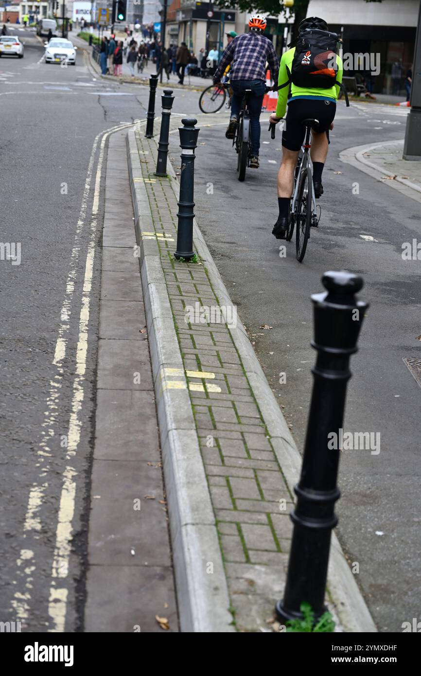 Two cyclists using dedicated cycle lane separated from road by bollards and concrete kerb in ...