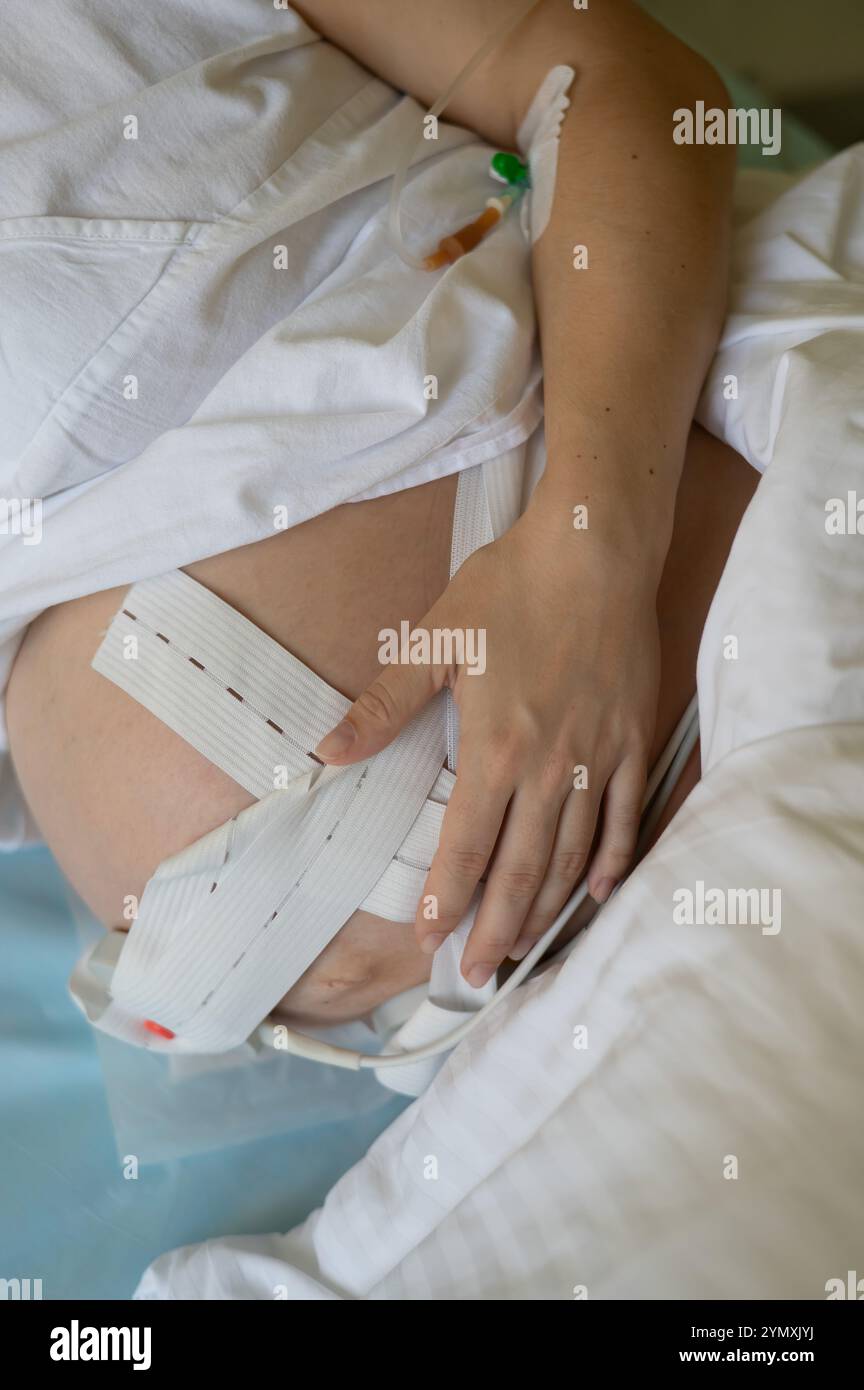 Close up of pregnant woman belly with cardiotocography sensor and IV in ...
