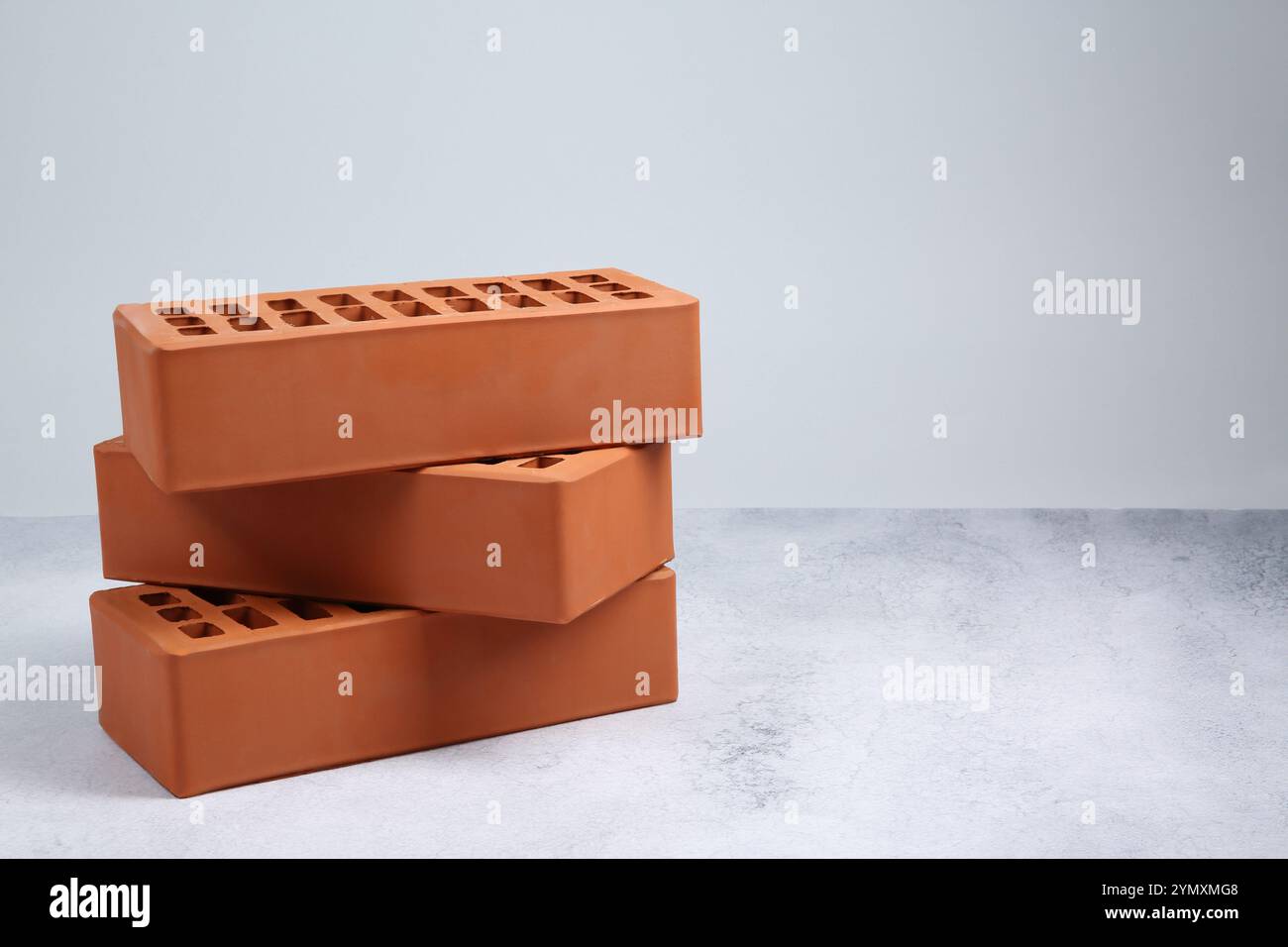 Three red bricks on textured table against light background, space for ...