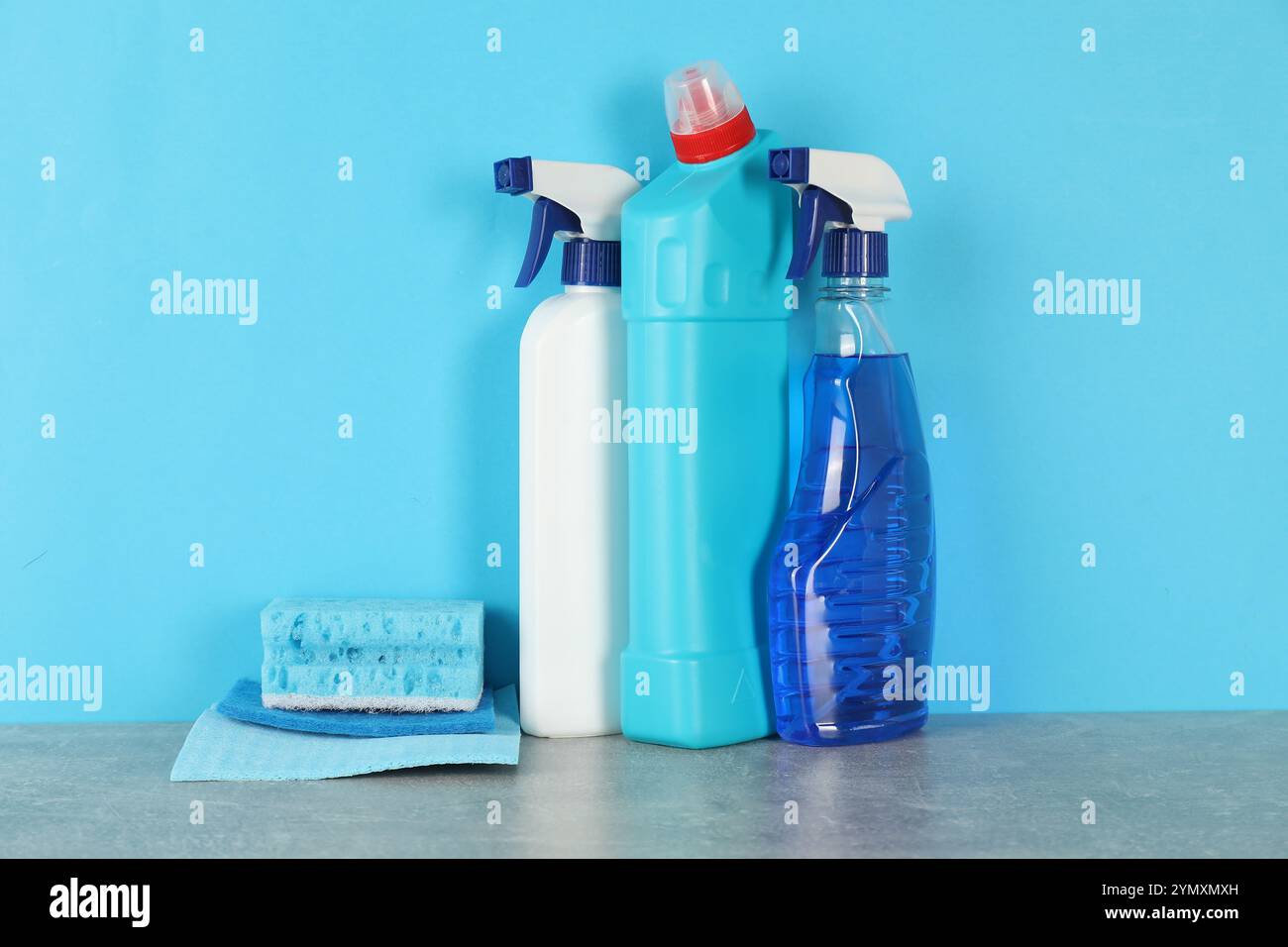 Different cleaning products and supplies on grey table against light ...