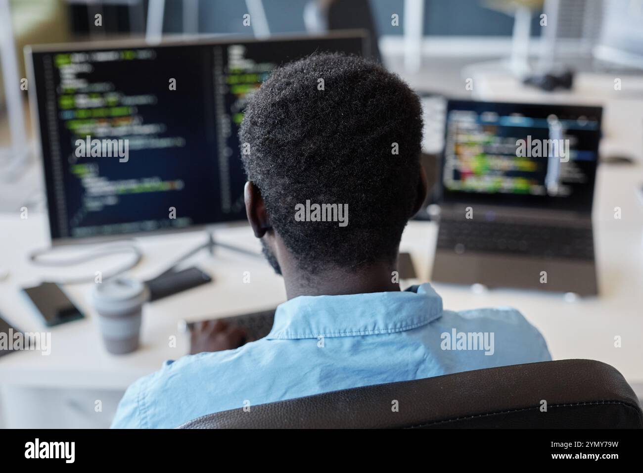 Black person seated at a desk, working on software development while surrounded by multiple ...