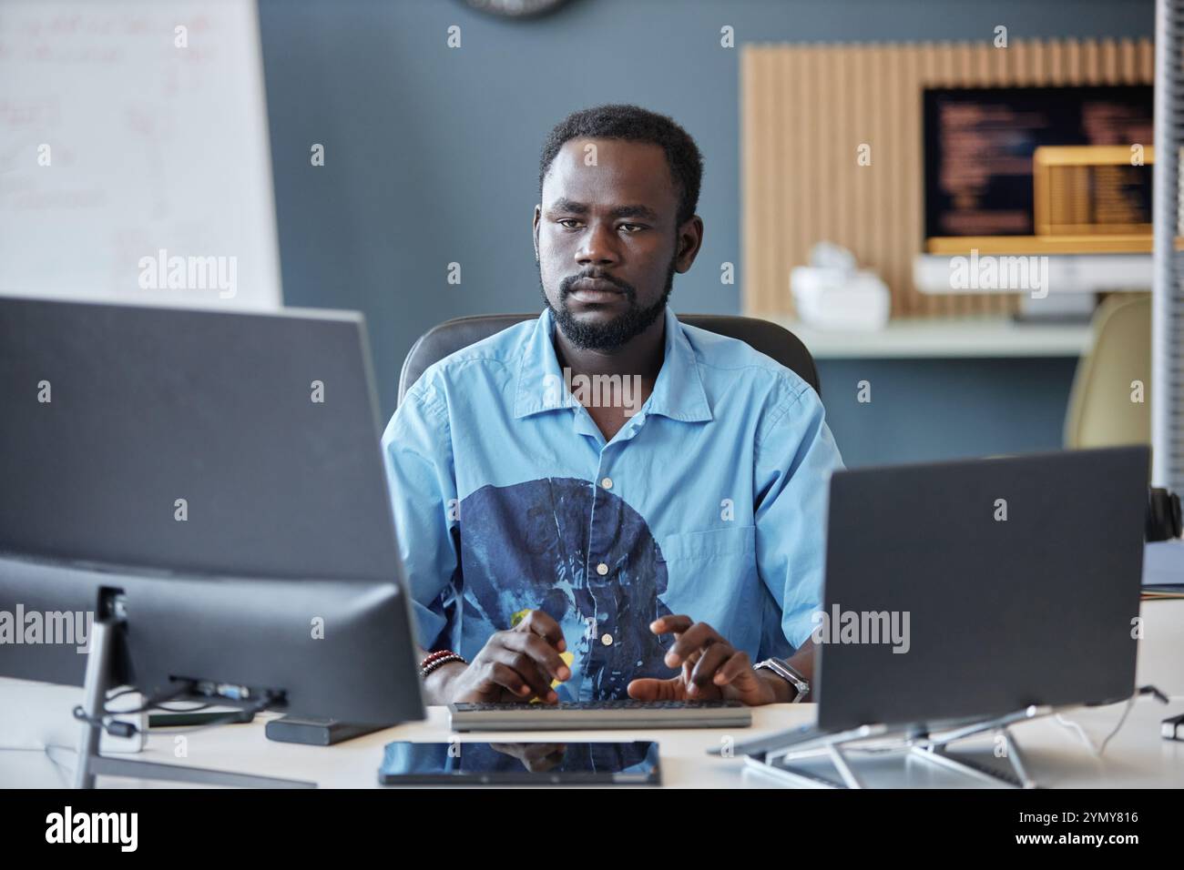 Man sitting at a desk and working with multiple computer screens ...